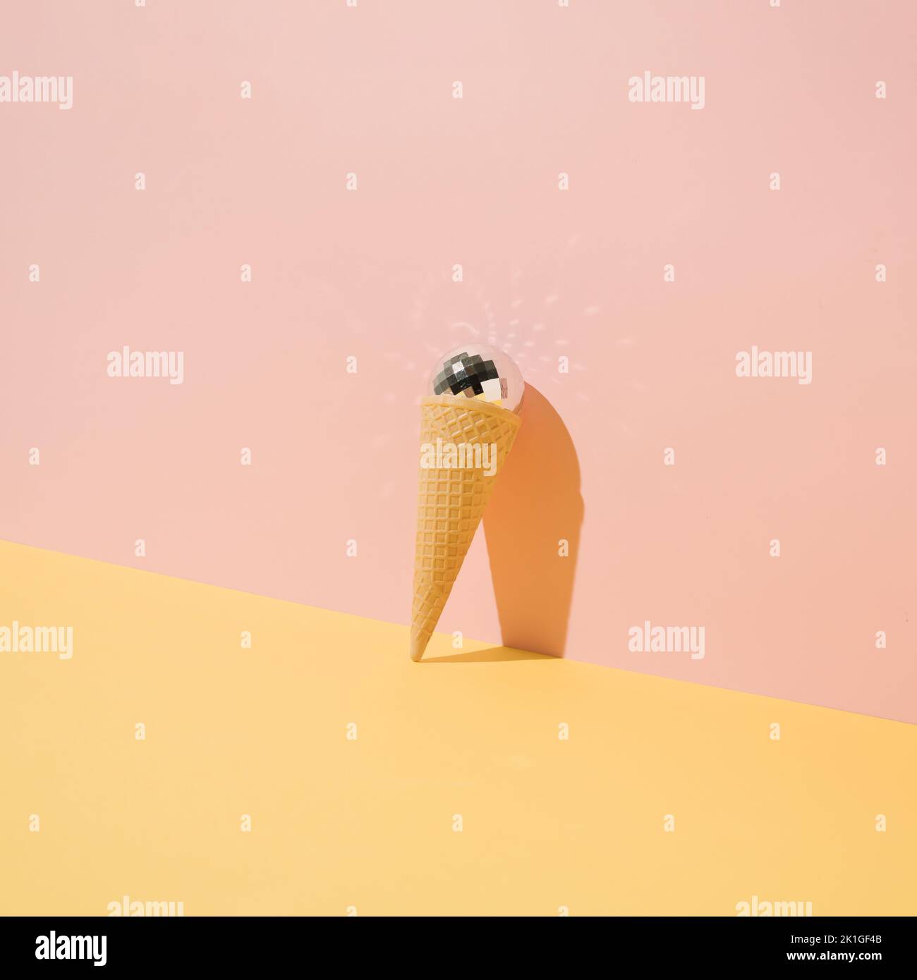 Ice cream cone with disco ball leaning on pink and yellow background ...