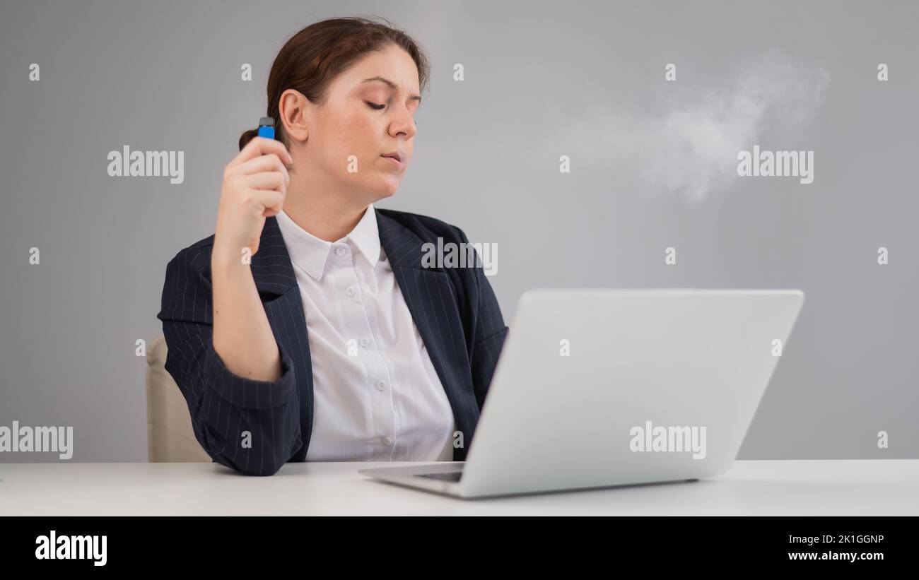 Business woman smoking a disposable vape while sitting at her desk ...