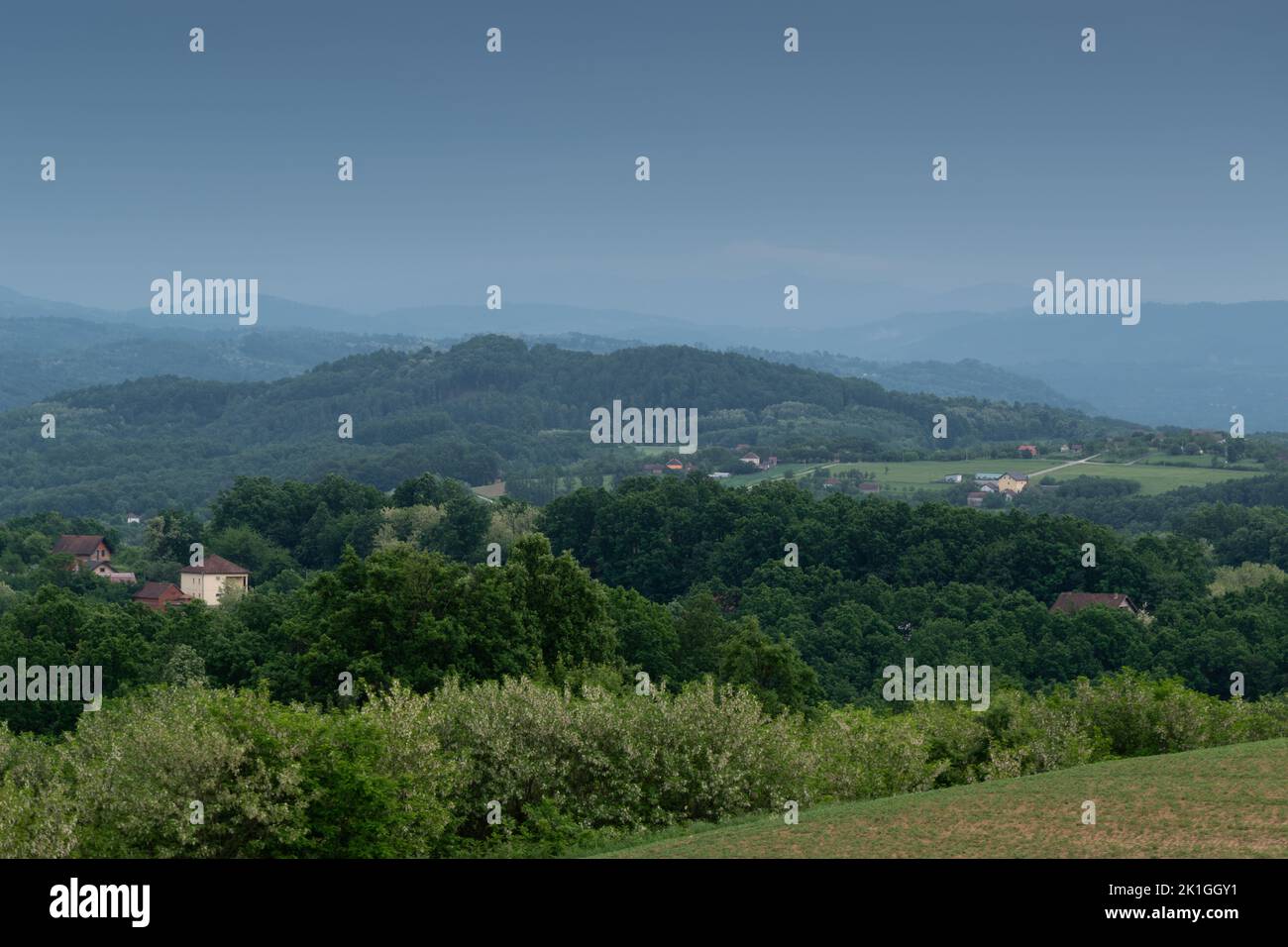 HIlly village with scattered houses and mountain in haze during gloomy ...