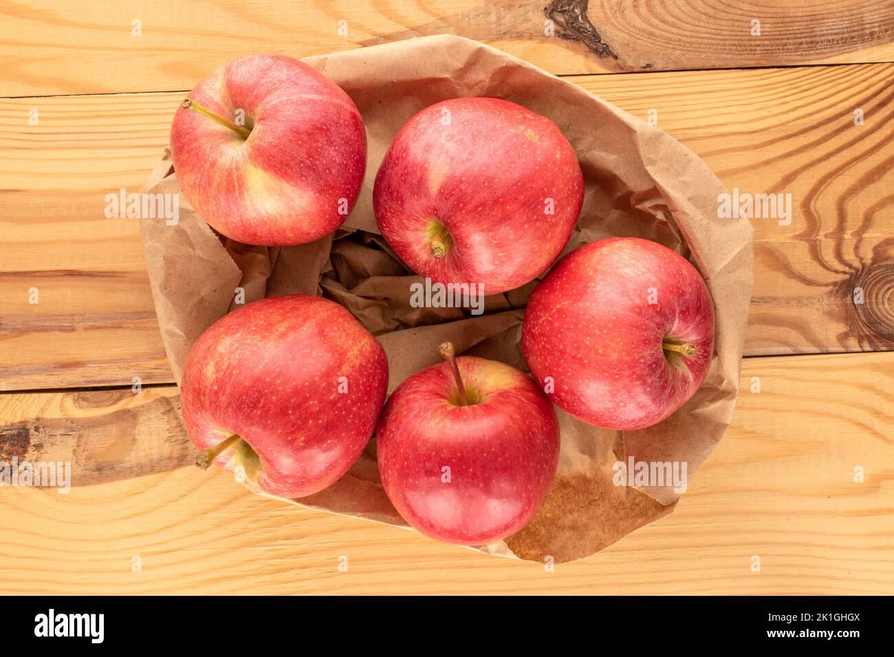 Several sweet red apples with paper bag on wooden table, macro, top ...