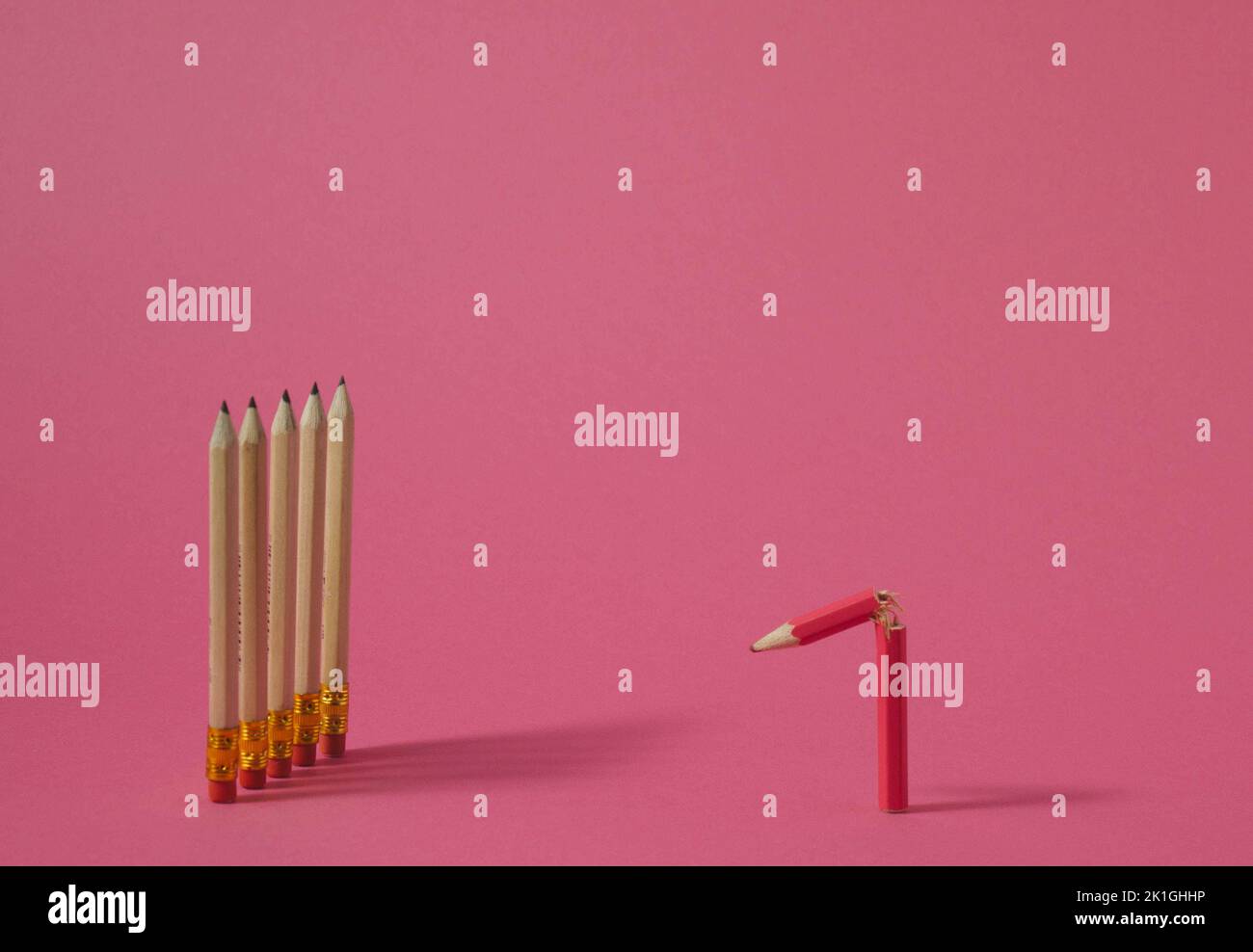 Broken pink wooden crayon in front of pencils on pink background ...