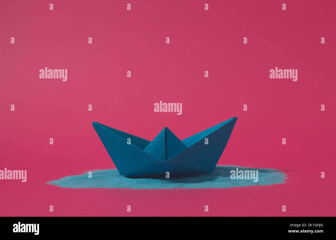 Blue origami paper boat floating on blue sand with pink background ...