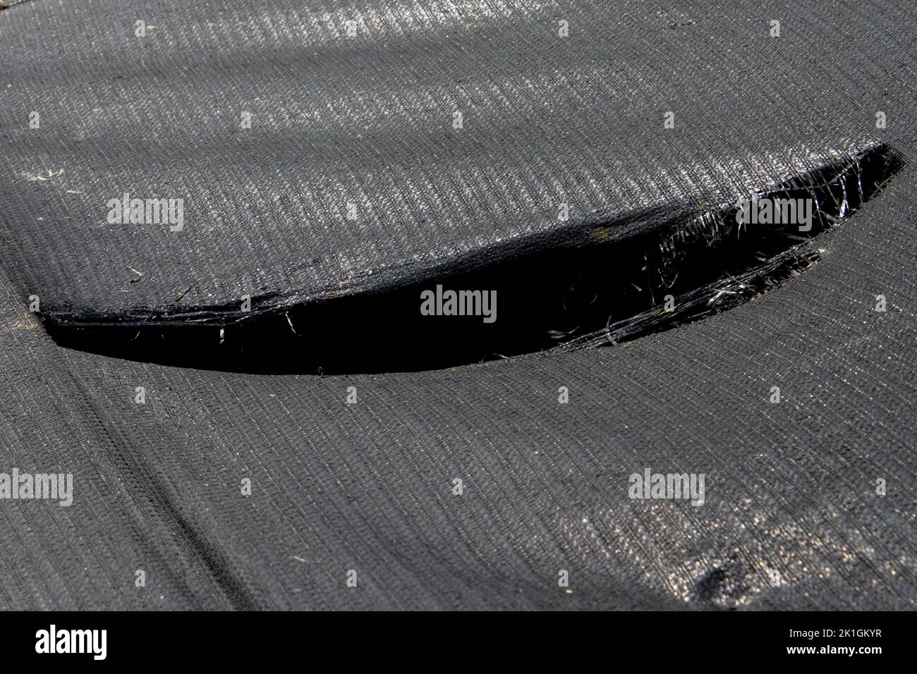 Hole torn in a black woven tarpaulin Stock Photo - Alamy