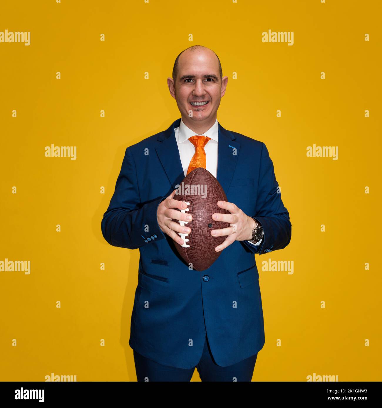 A bald Caucasian man dressed in a blue suit, white shirt and orange tie ...