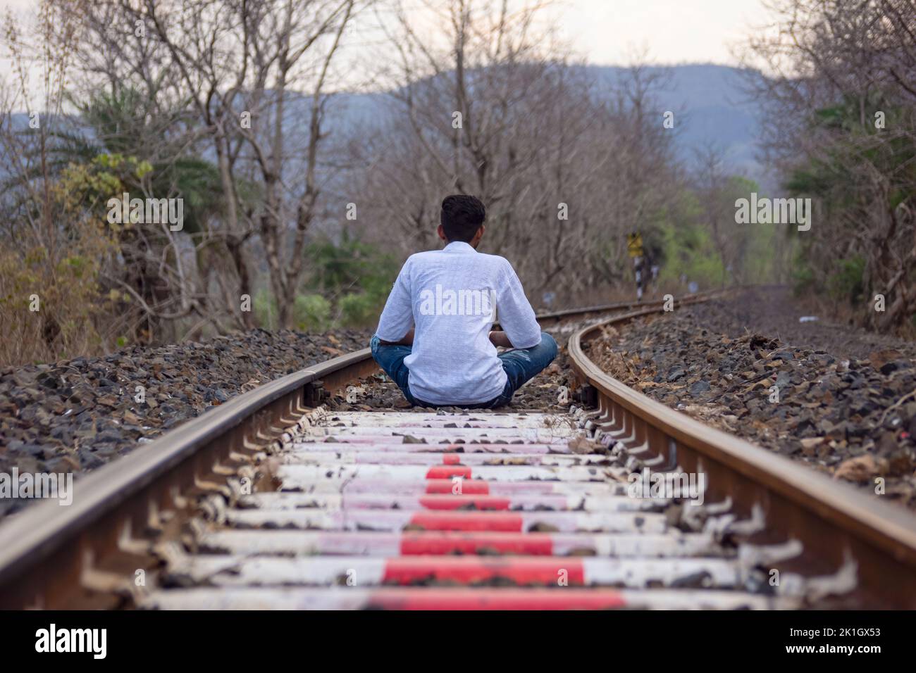 A man sitting on railway track in meditating pose at mountain village ...