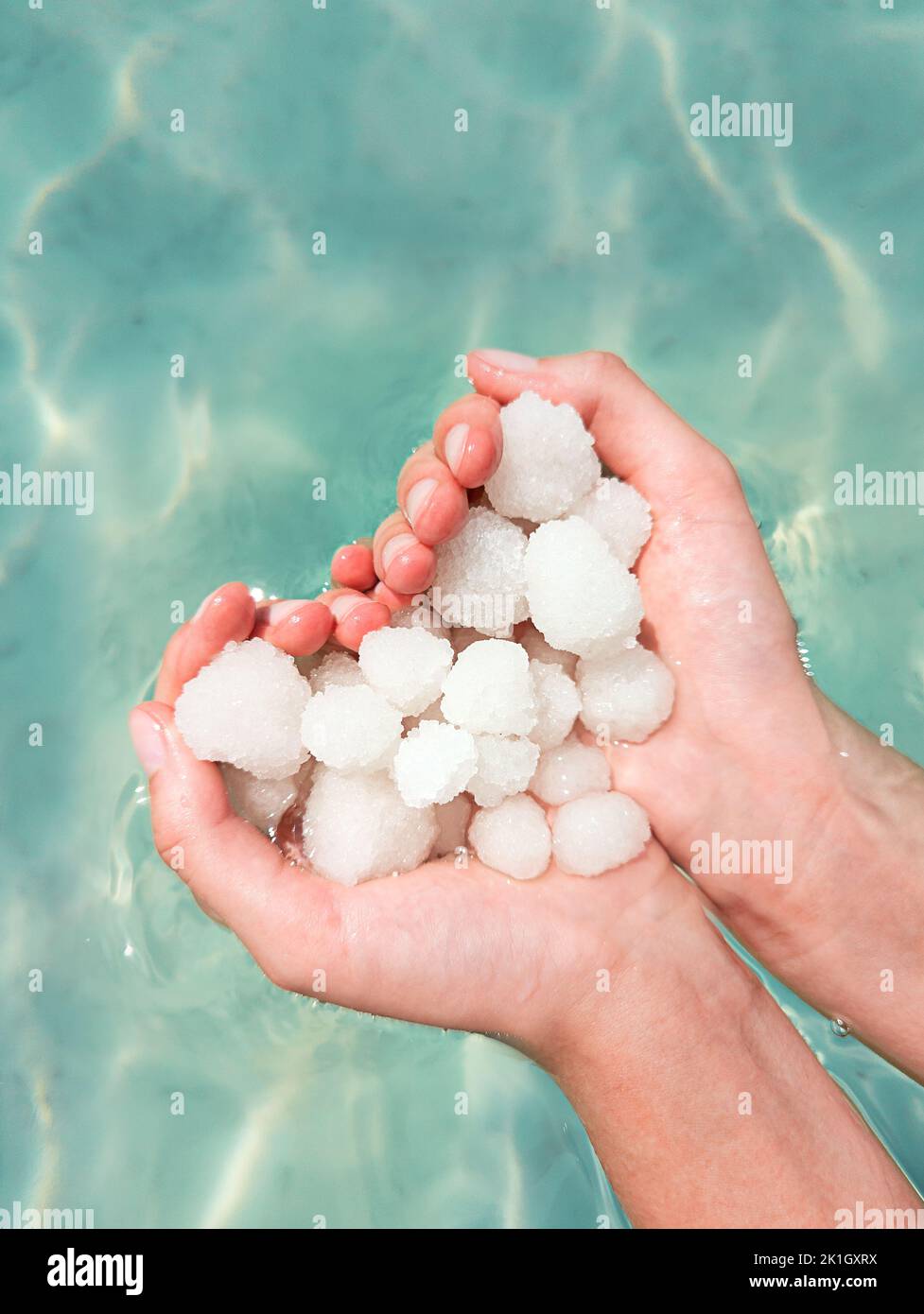Hands holding sea salt crystals heart-saped on sea water background ...