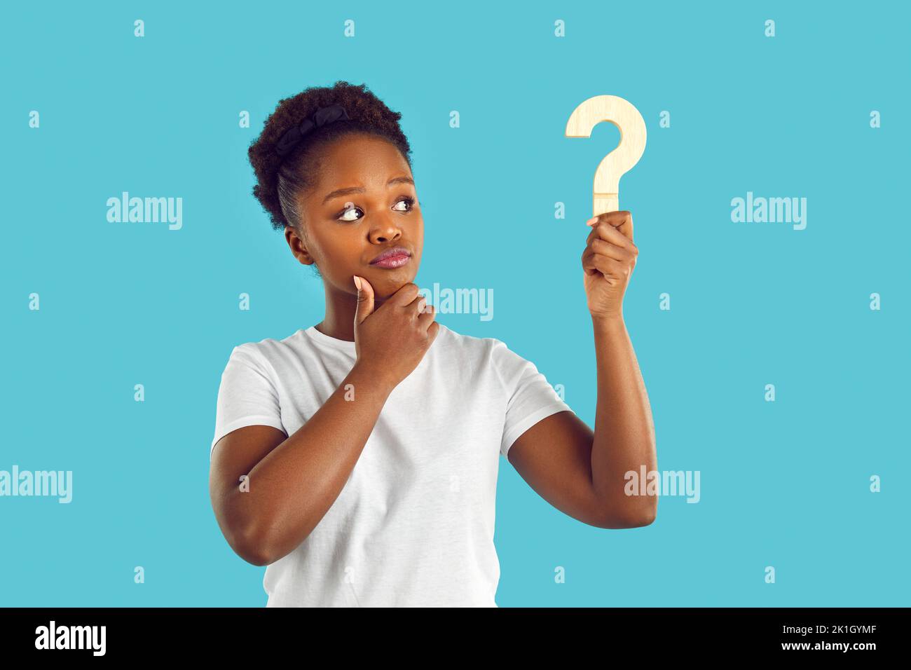 Young dark skinned woman with doubtful expression is looking at wooden ...