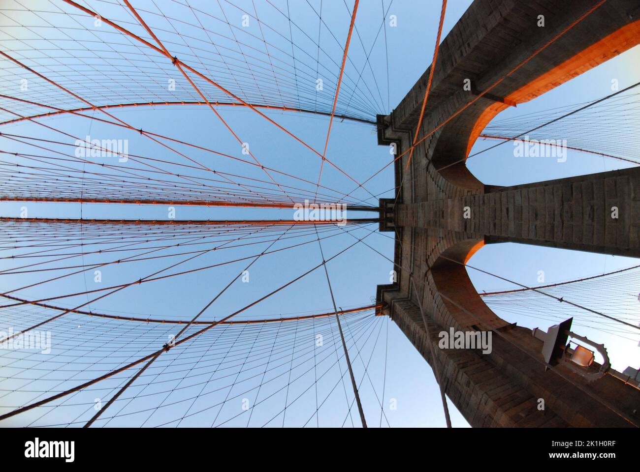 A low angle of Wire ropes of the Brooklyn Bridge against a blue sky in ...
