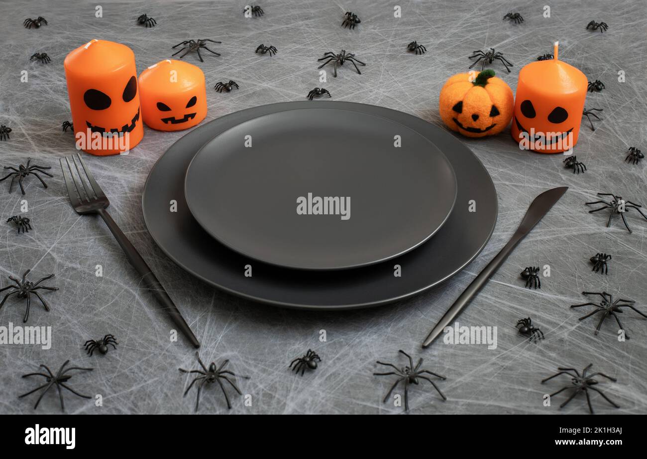 Halloween table setting with black dishes. Empty plate, orange candles ...