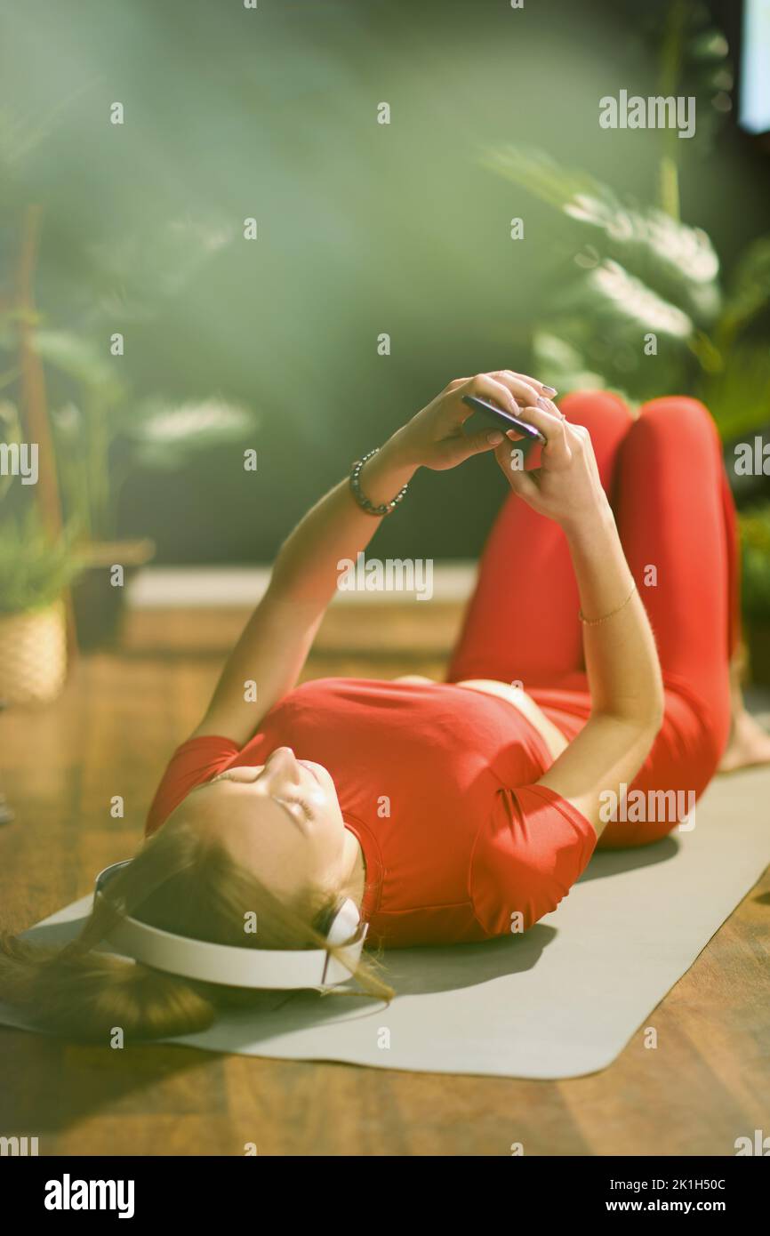 young female in red fitness clothes with yoga mat using smartphone and ...