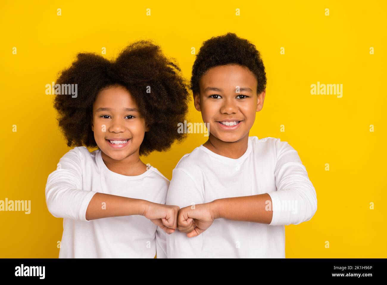 Portrait of two positive buddies give fist bump each other toothy smile isolated on yellow color ...