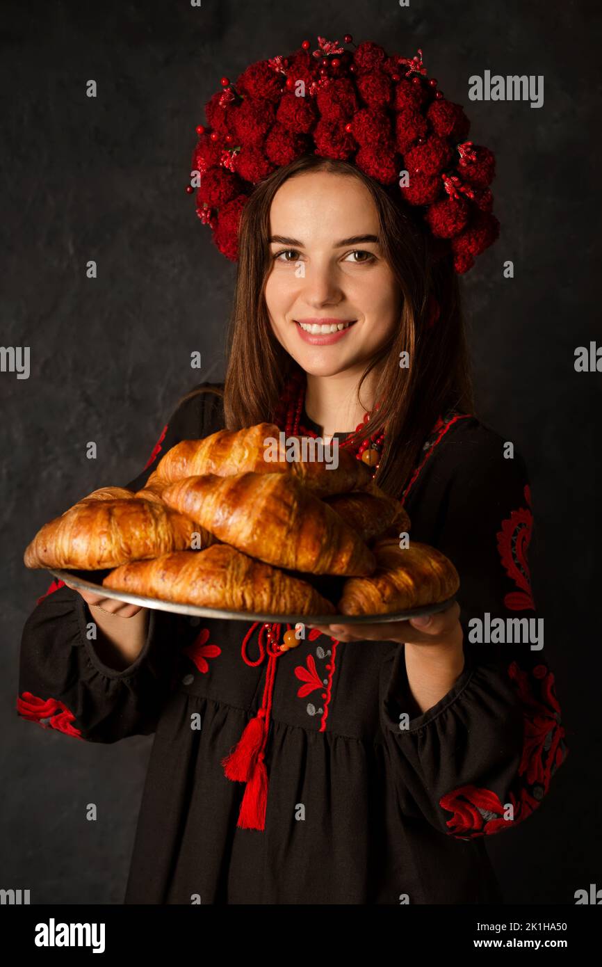 A beautiful young woman in Ukrainian clothes holds croissants on a tray ...