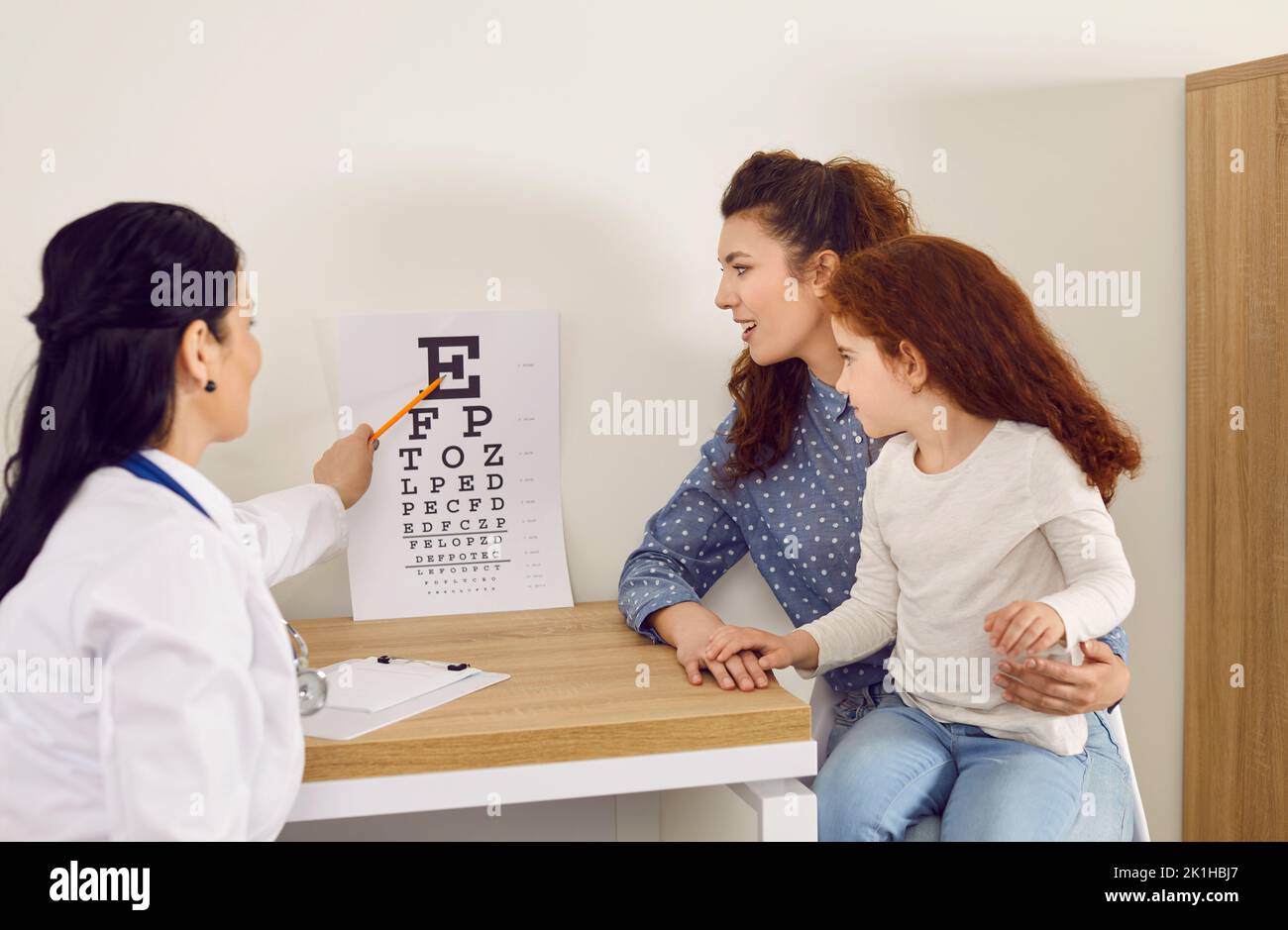 Female optometrist with test chart checks kid eye sight who came to ...