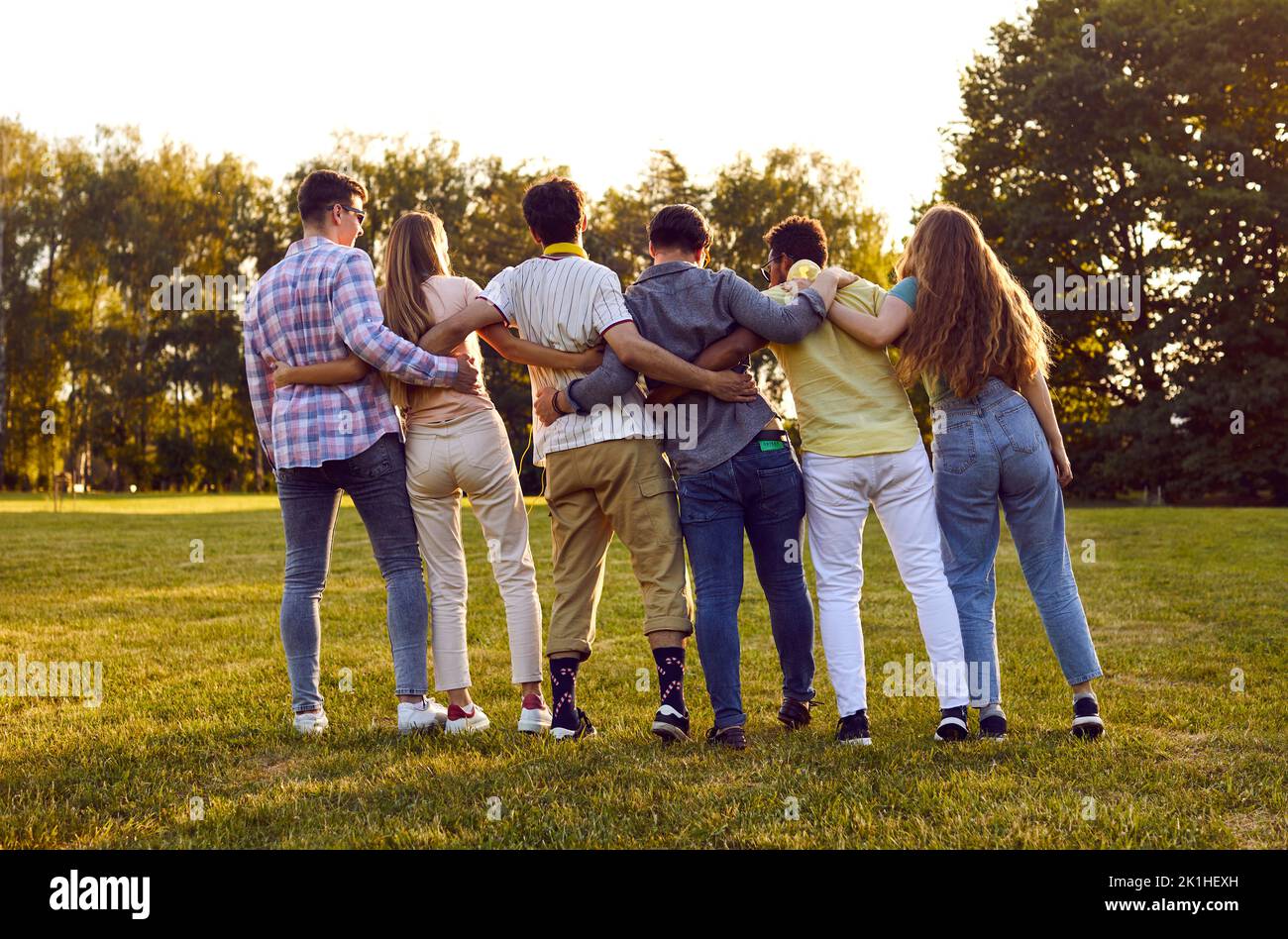 Back view of diverse friends standing in green summer park and hugging ...