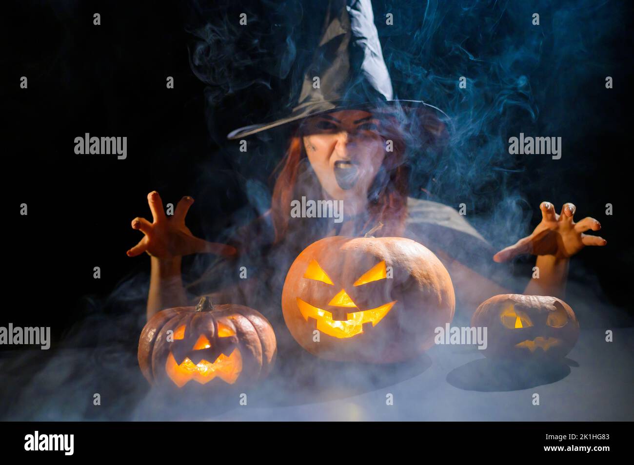 An ominous witch in a hat conjures over a jack-o-lantern. Traditional ...