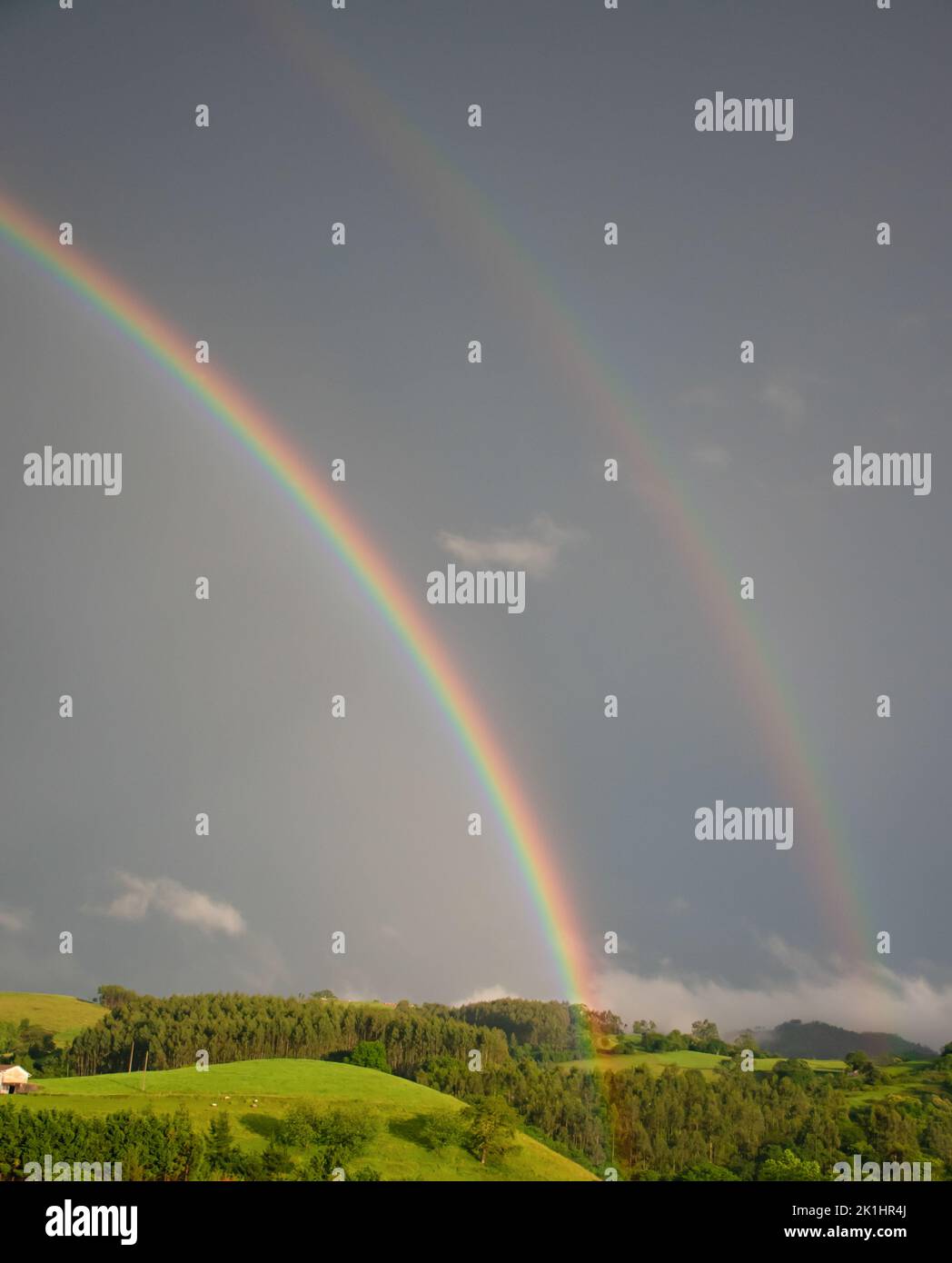 A rainbow and its reflection in a landscape of green meadows in ...