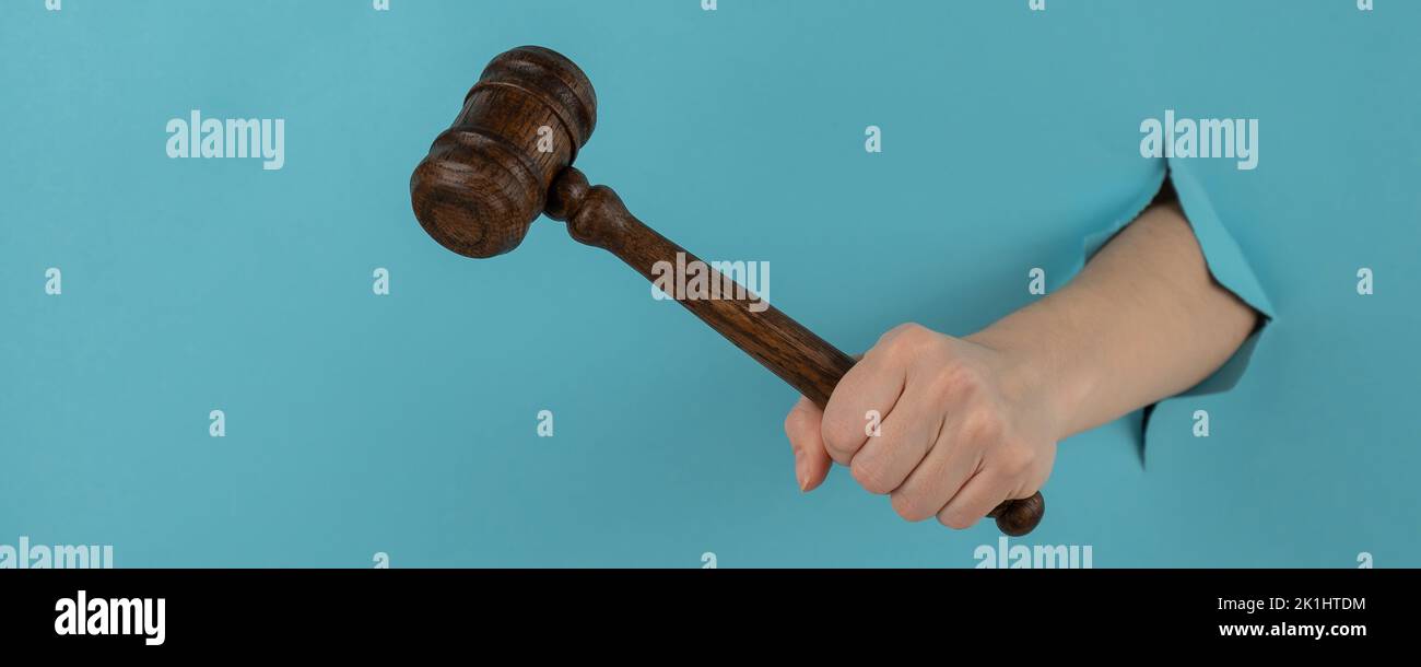 A woman's hand with a wooden judge's gavel sticks out of a hole in a ...