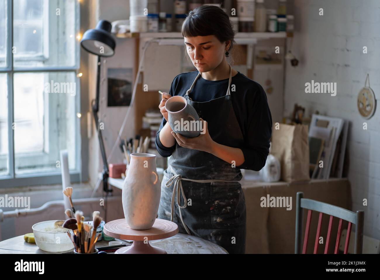 Serious craftswoman draws sketch on grey vase with thoughtful ...