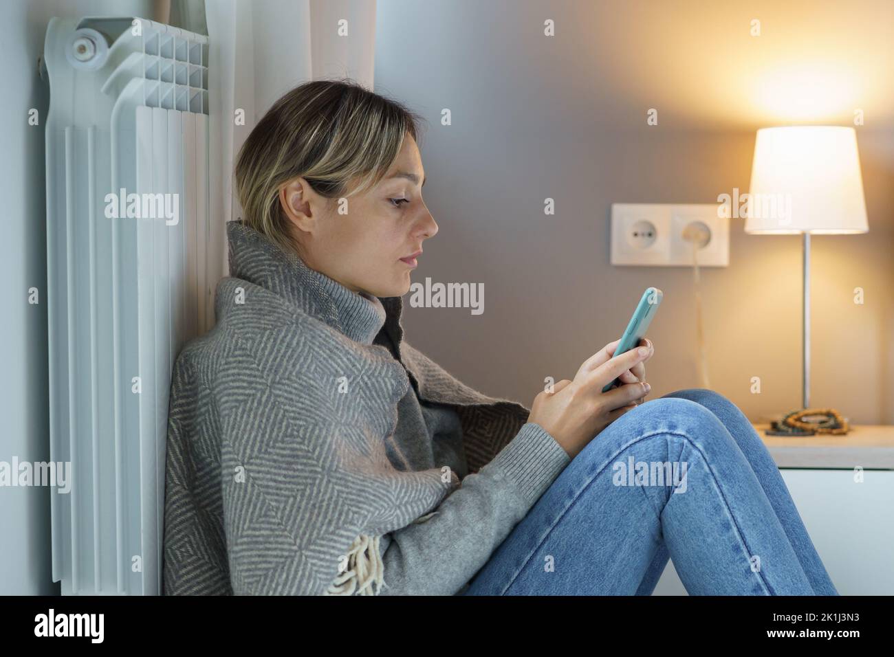 Tired blonde woman snuggling up to battery scrolls smartphone looking ...