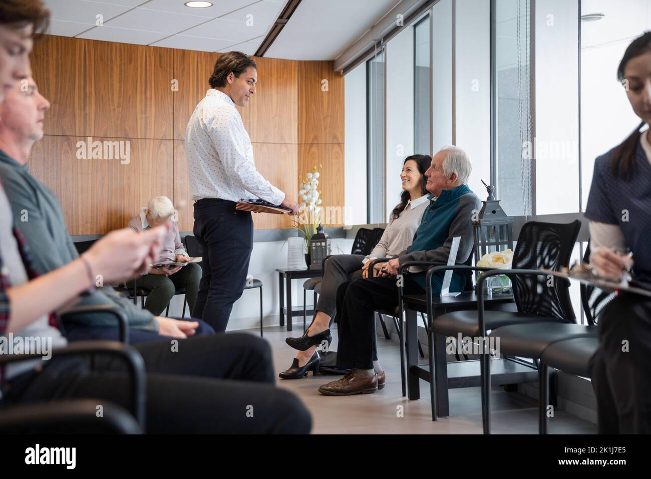 Doctors talking to patients in waiting area of community medical center ...