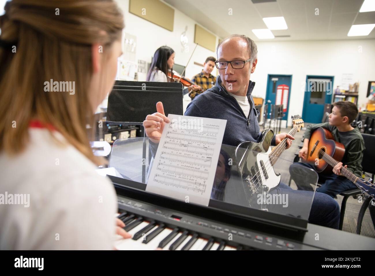 Junior high teacher guiding student playing electric piano in classroom ...