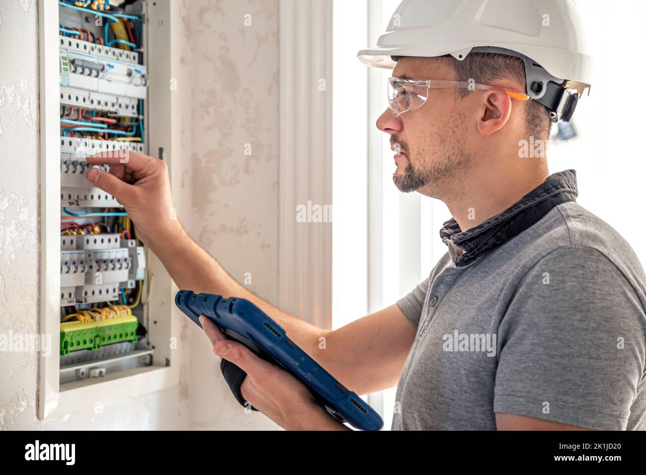 Man, an electrical technician working in a switchboard with fuses, uses ...