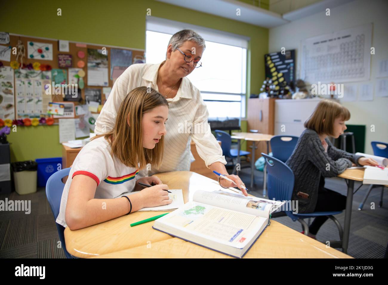 Female junior high teacher helping student with homework in classroom ...