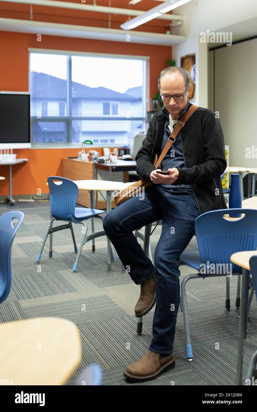 Male junior high teacher using smart phone in classroom Stock Photo - Alamy