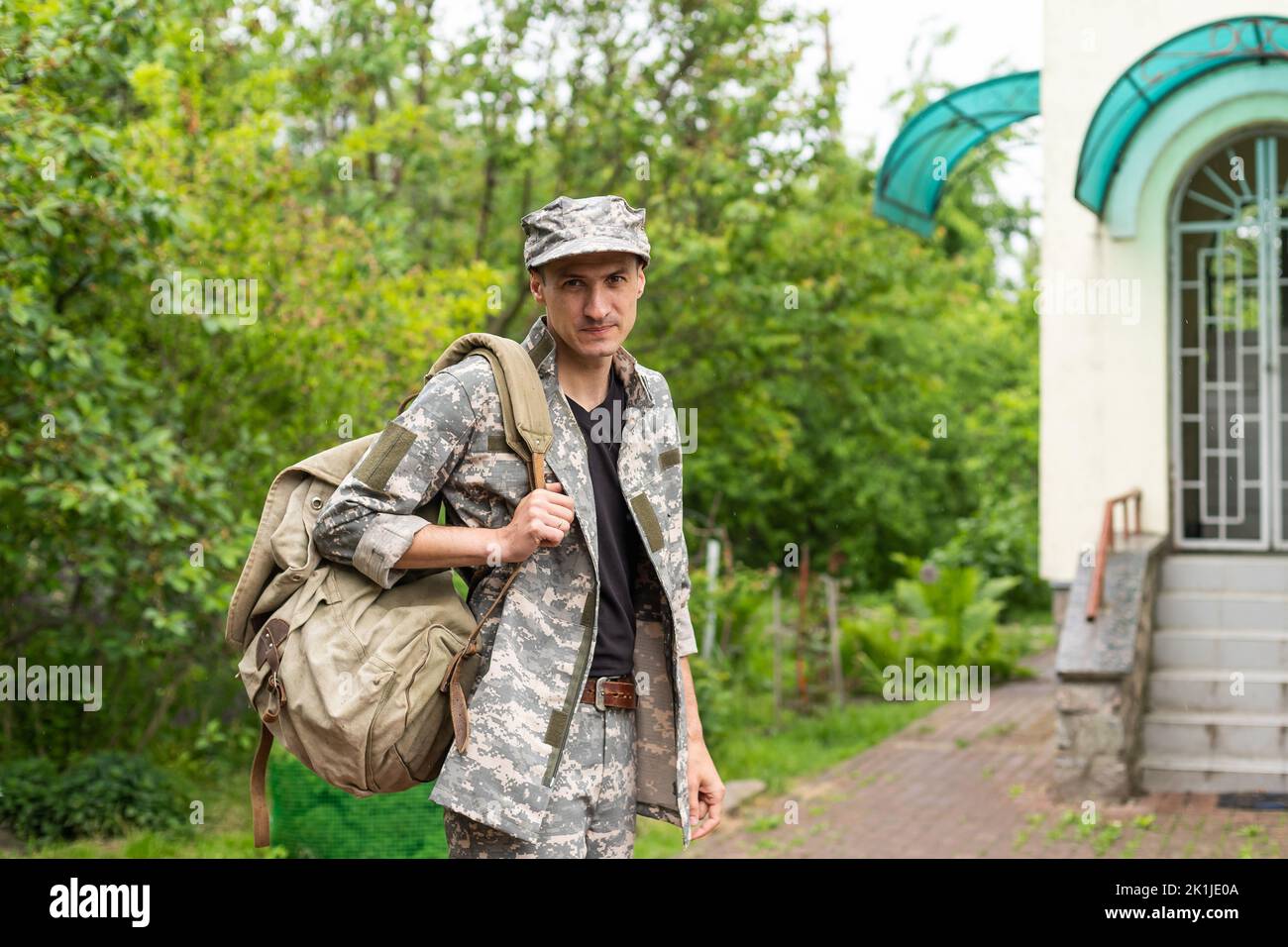 Photo of soldier in camouflaged uniform holding olive colored backpack ...