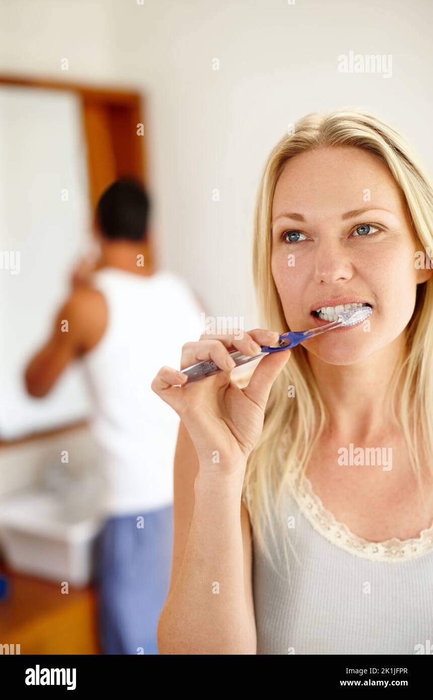 Getting ready together. A woman brushing her teeth while her boyfriend ...