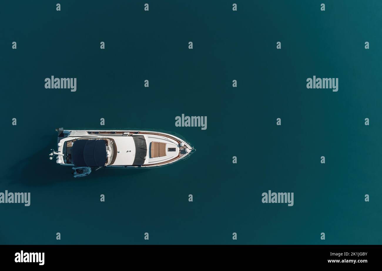 Aerial yacht on calm sea. Luxury cruise trip. View from above of white boat on deep blue water ...