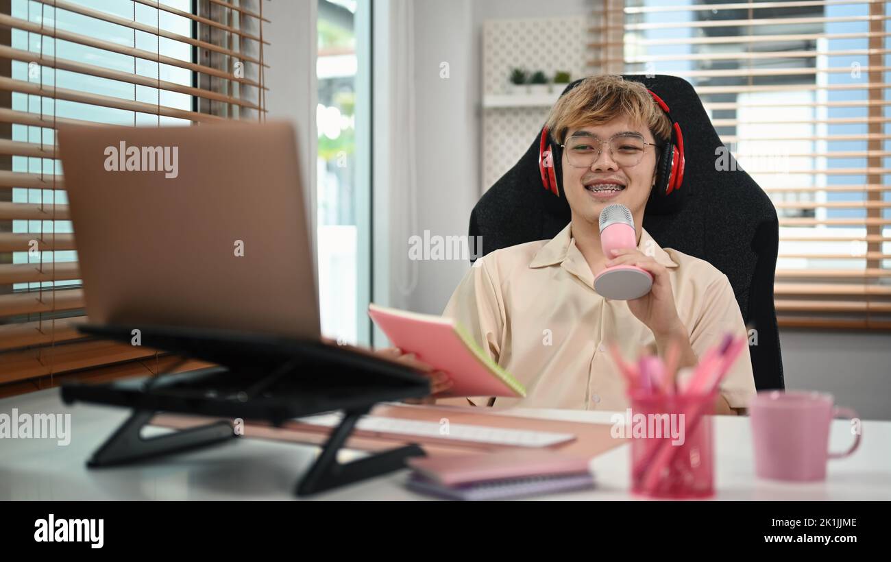 Asian male using microphone and laptop computer streaming audio podcast ...