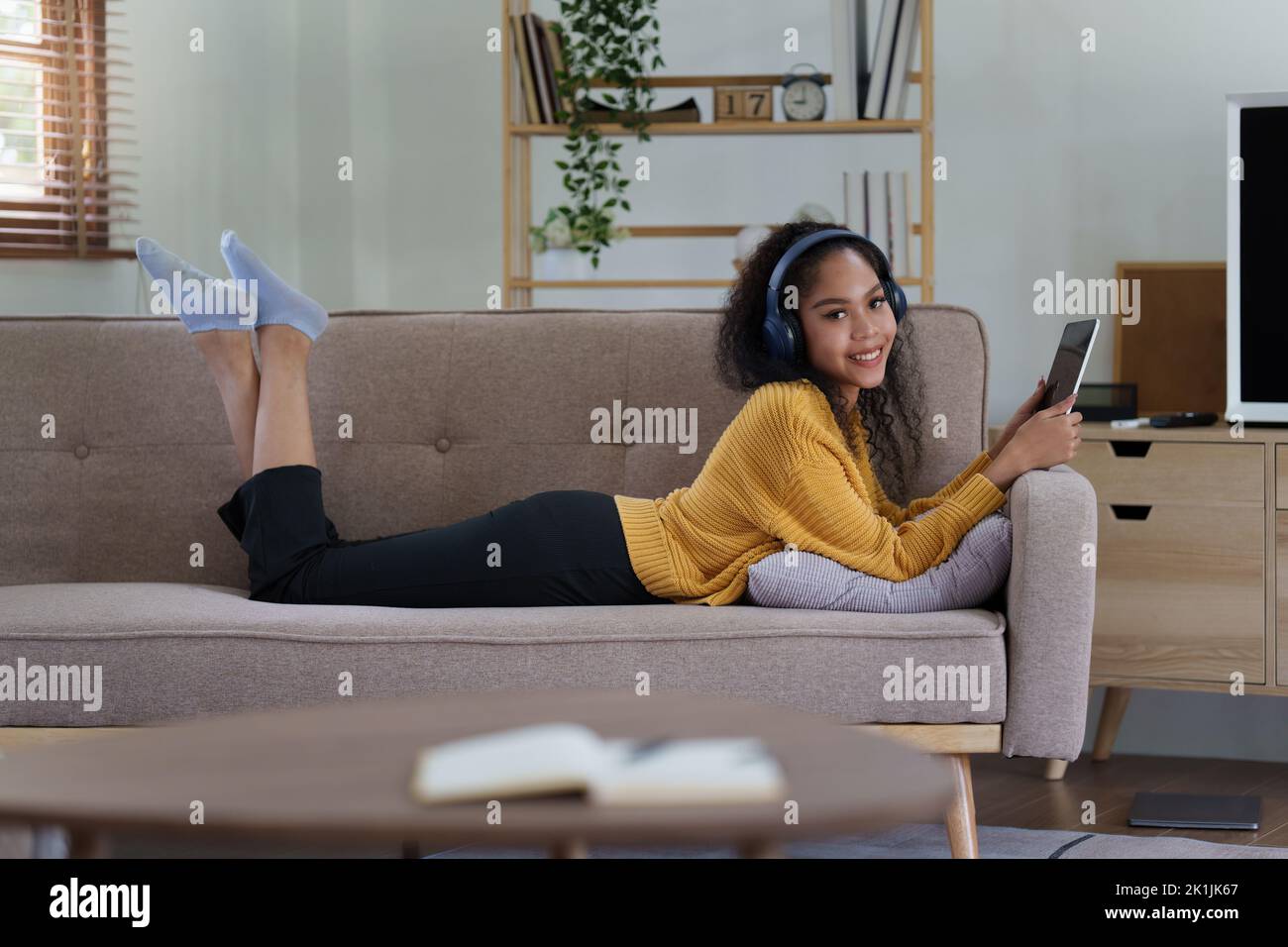 Attractive smiling young woman using tablet and listen music on sofa at ...