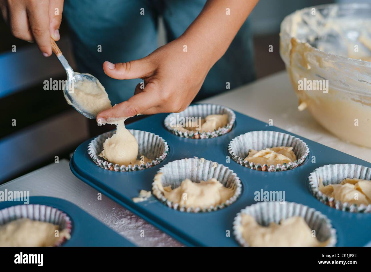 Close-up view of kid's hands, filling cupcake forms with dough ...