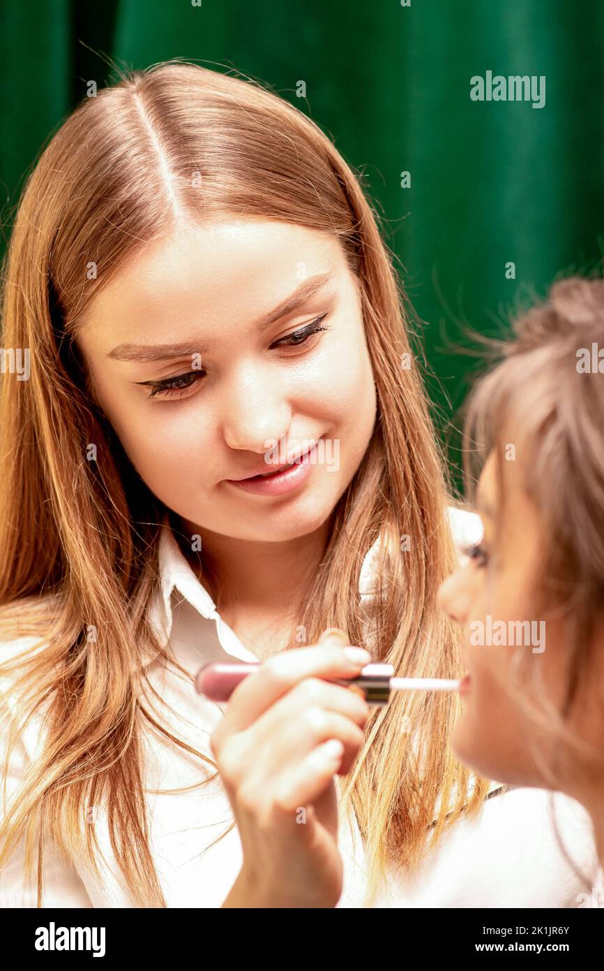 Makeup in the process. The makeup artist applies pink gloss lipstick on ...