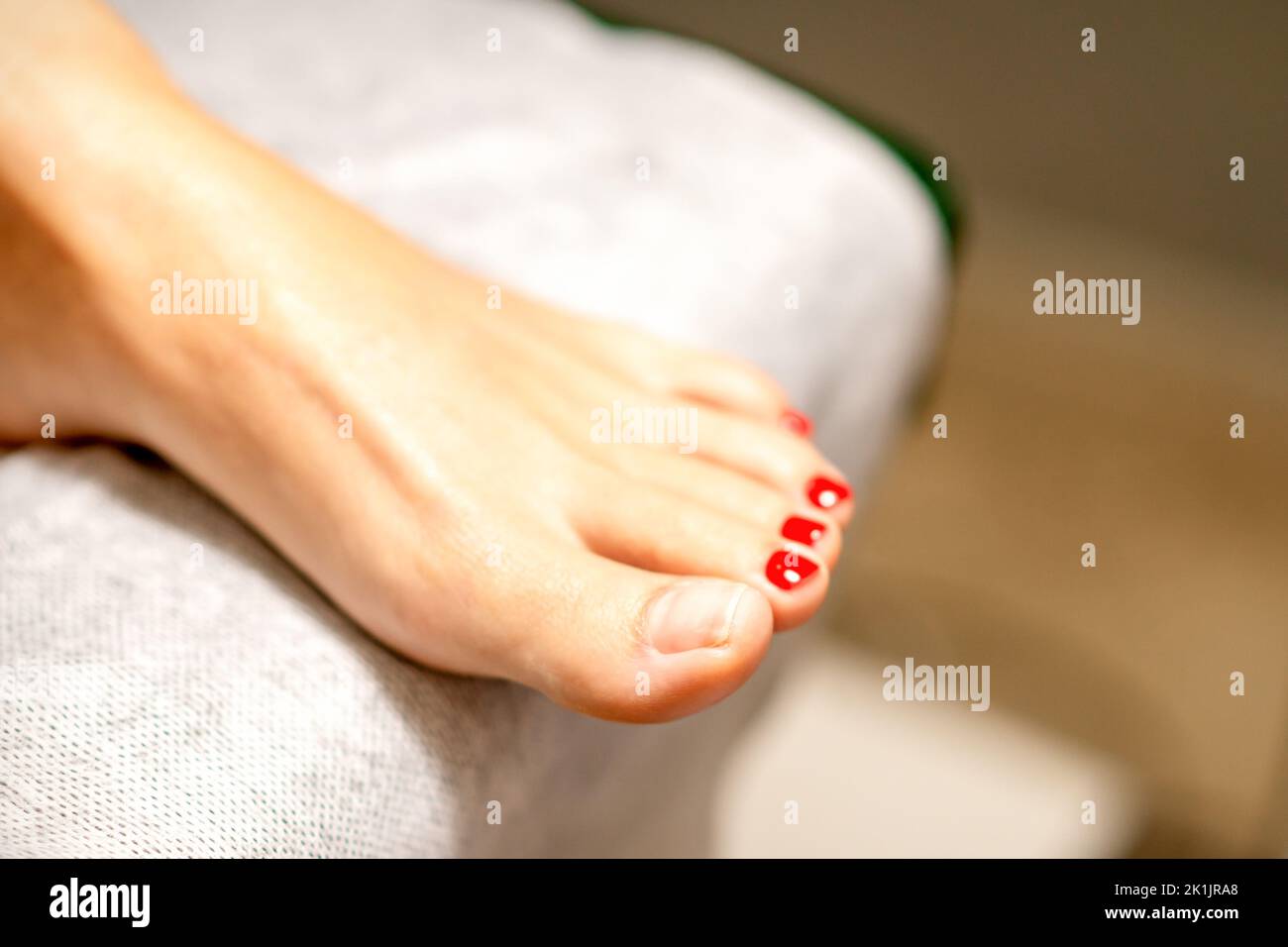 Nail painting process. Red painted fingernails on a female leg in a ...