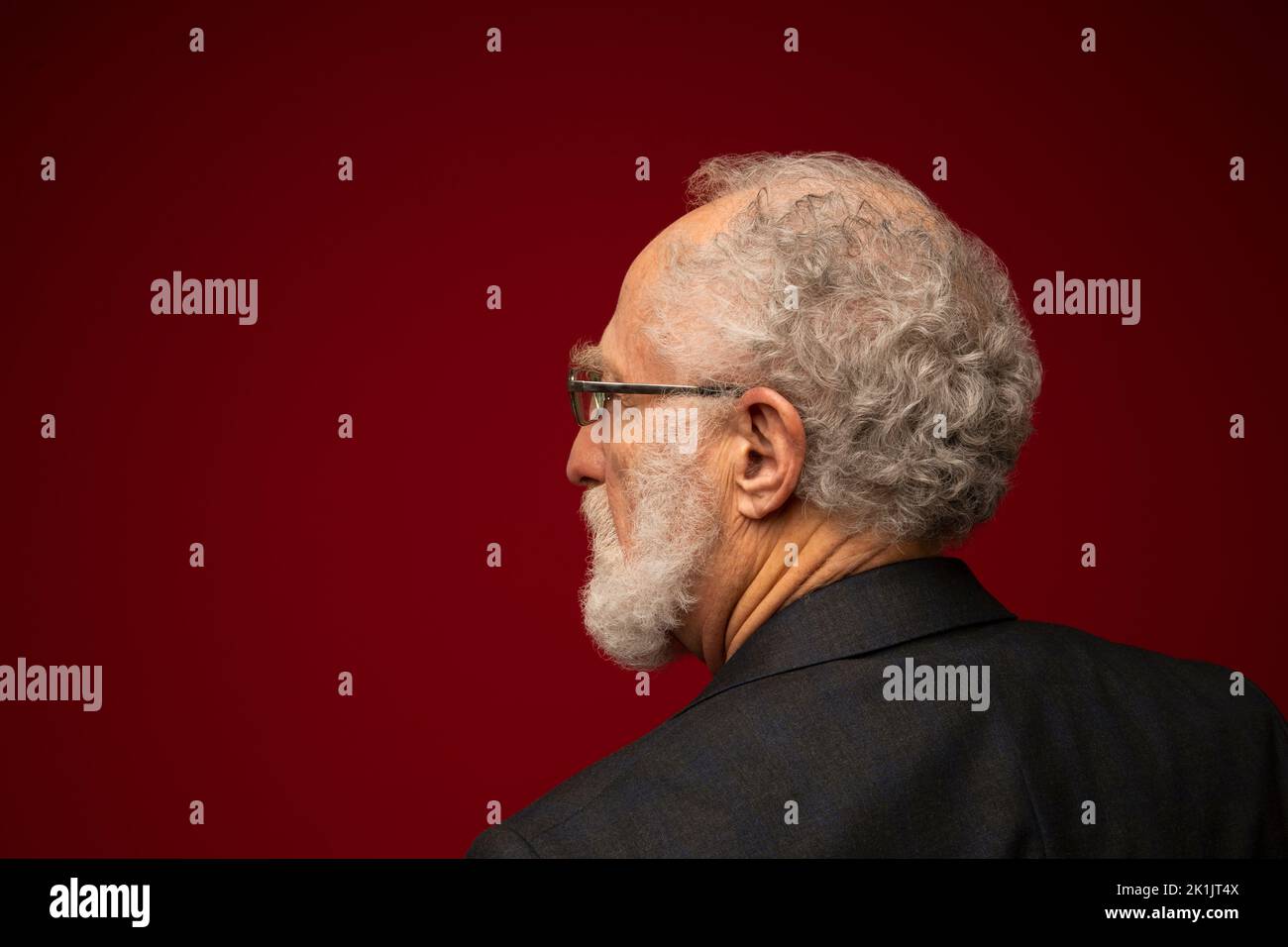 Portrait of senior man with curly gray hair and beard looking away ...