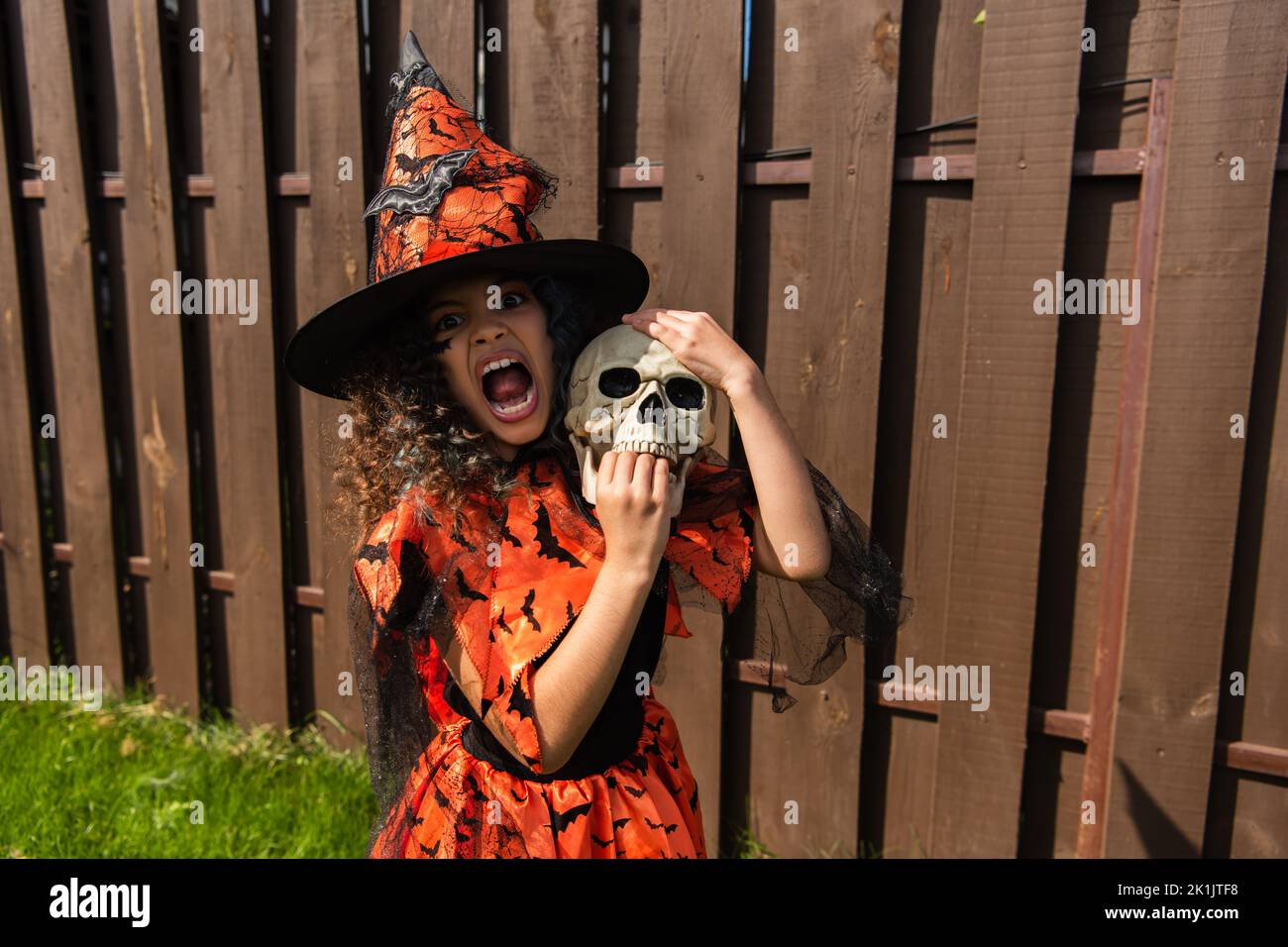 child in witch costume holding scary skull, grimacing and growling ...