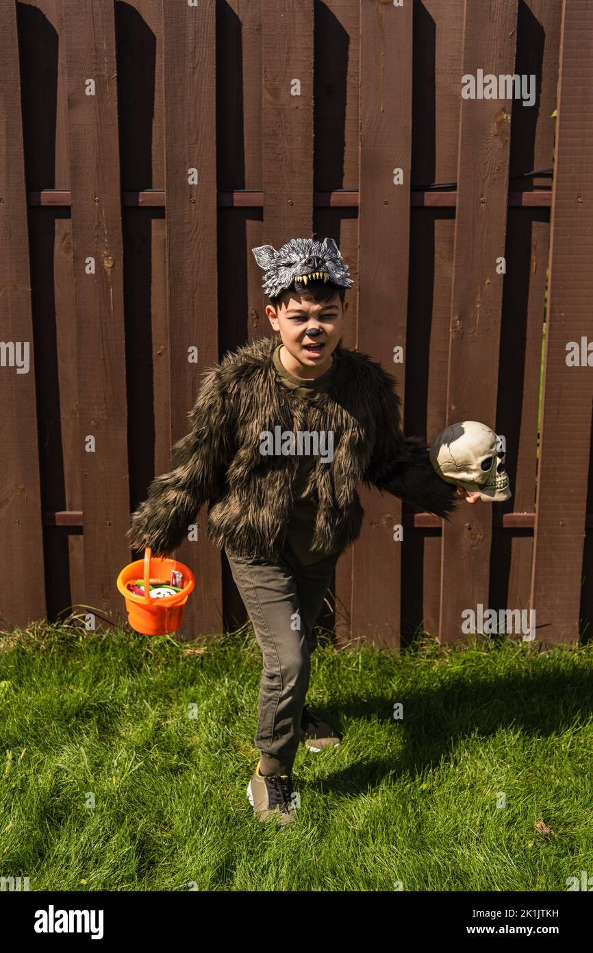 full length of asian boy in werewolf costume running with skull and ...