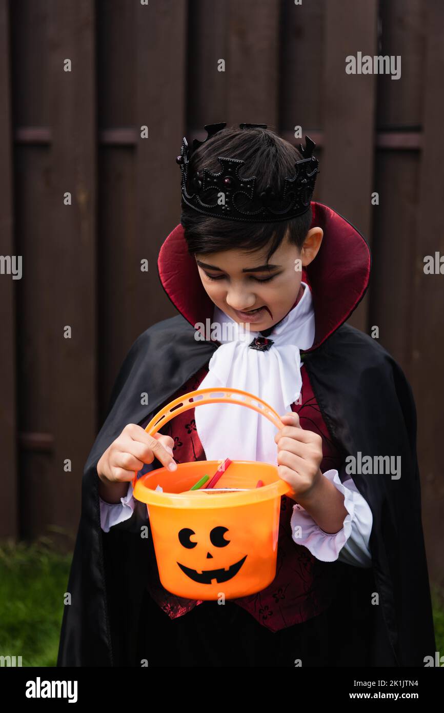 asian kid in vampire king costume looking into trick or treat bucket ...