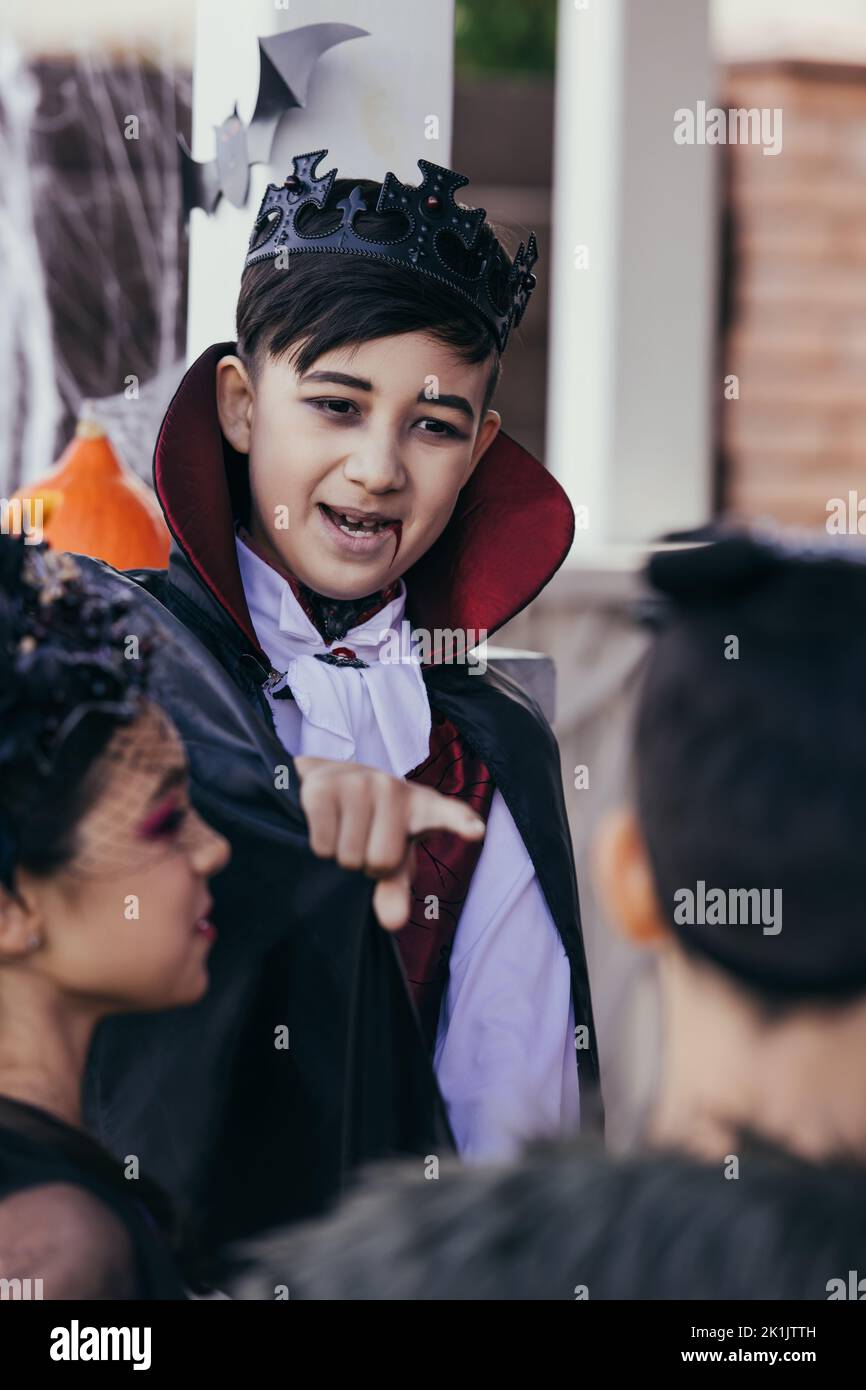 Asian boy in halloween vampire costume pointing with finger at blurred ...