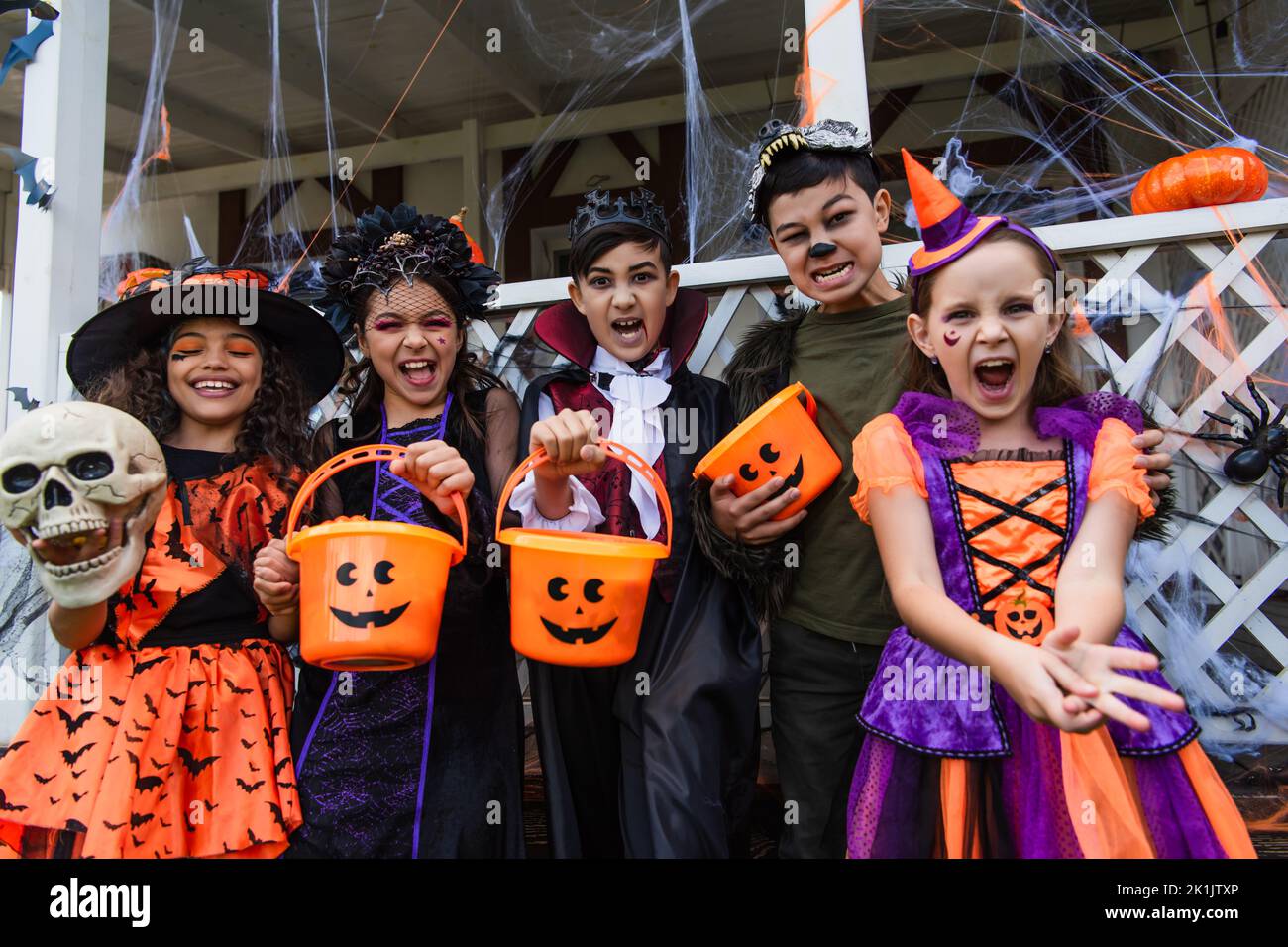 Smiling interracial kids grimacing and holding halloween buckets ...