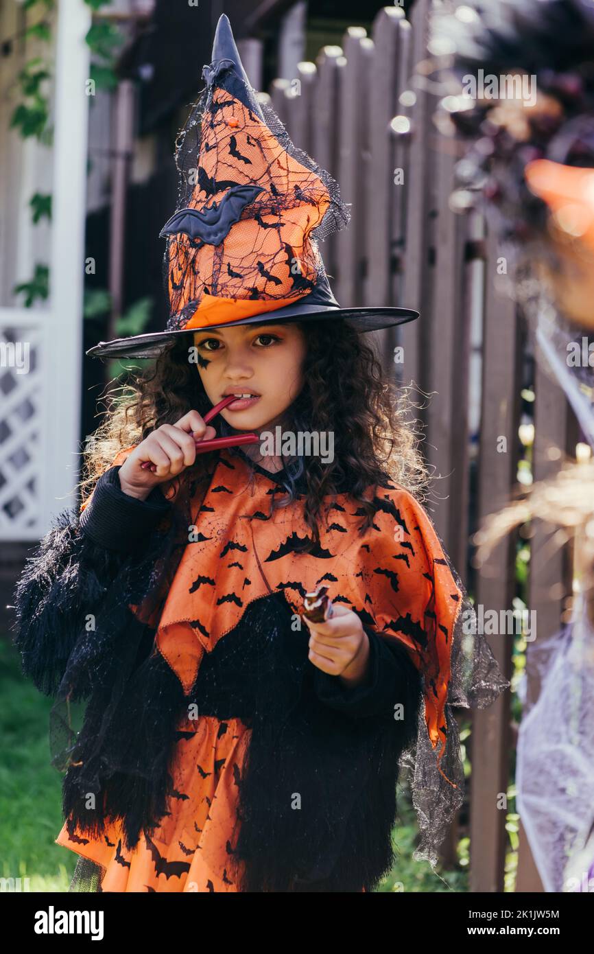 Preteen girl in witch hat eating candy during halloween celebration ...