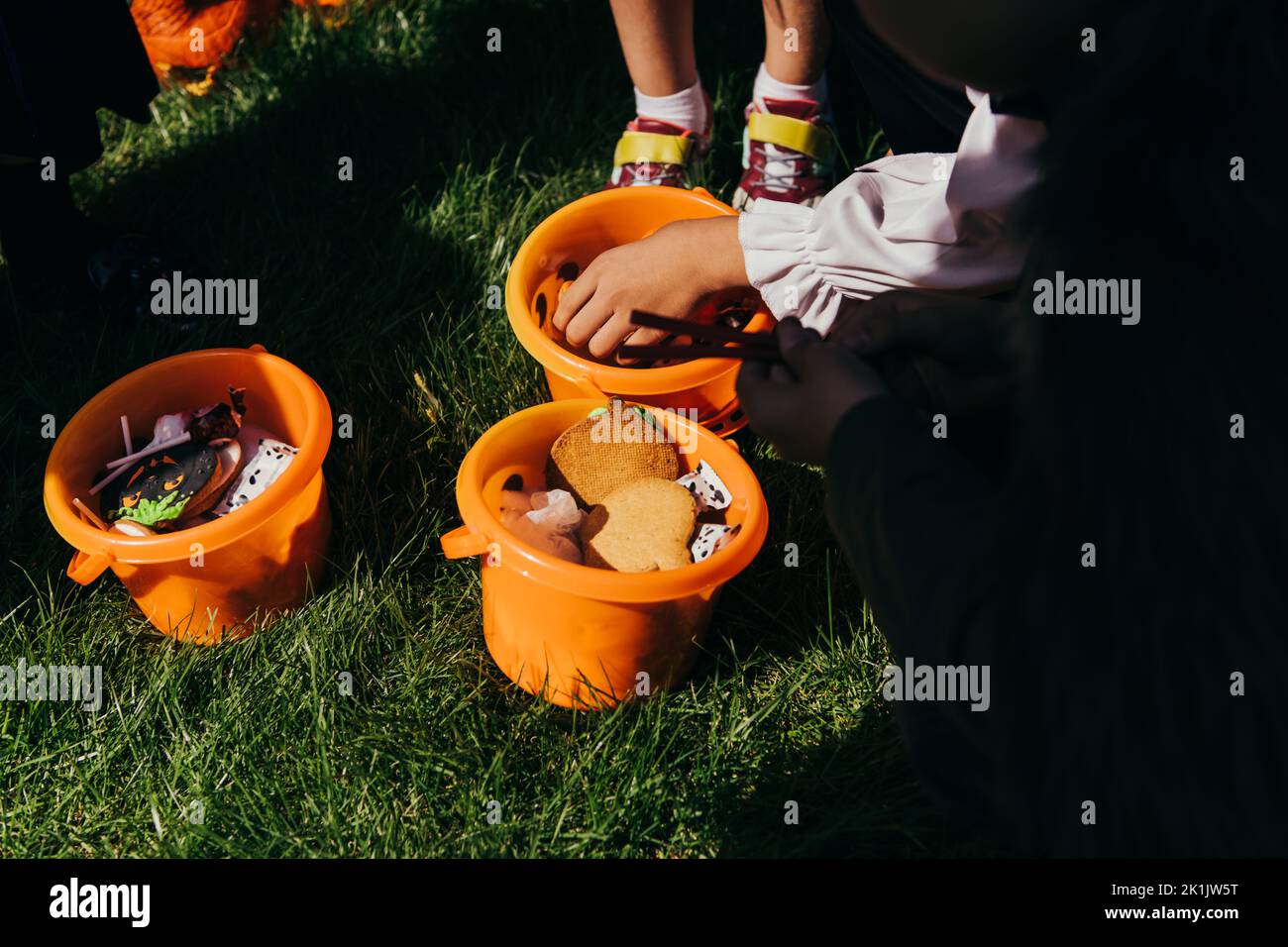 Cropped view of child taking candies from bucket during halloween party ...