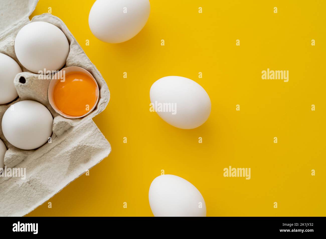 Top view of eggs near fresh yolk in shell in container on yellow ...