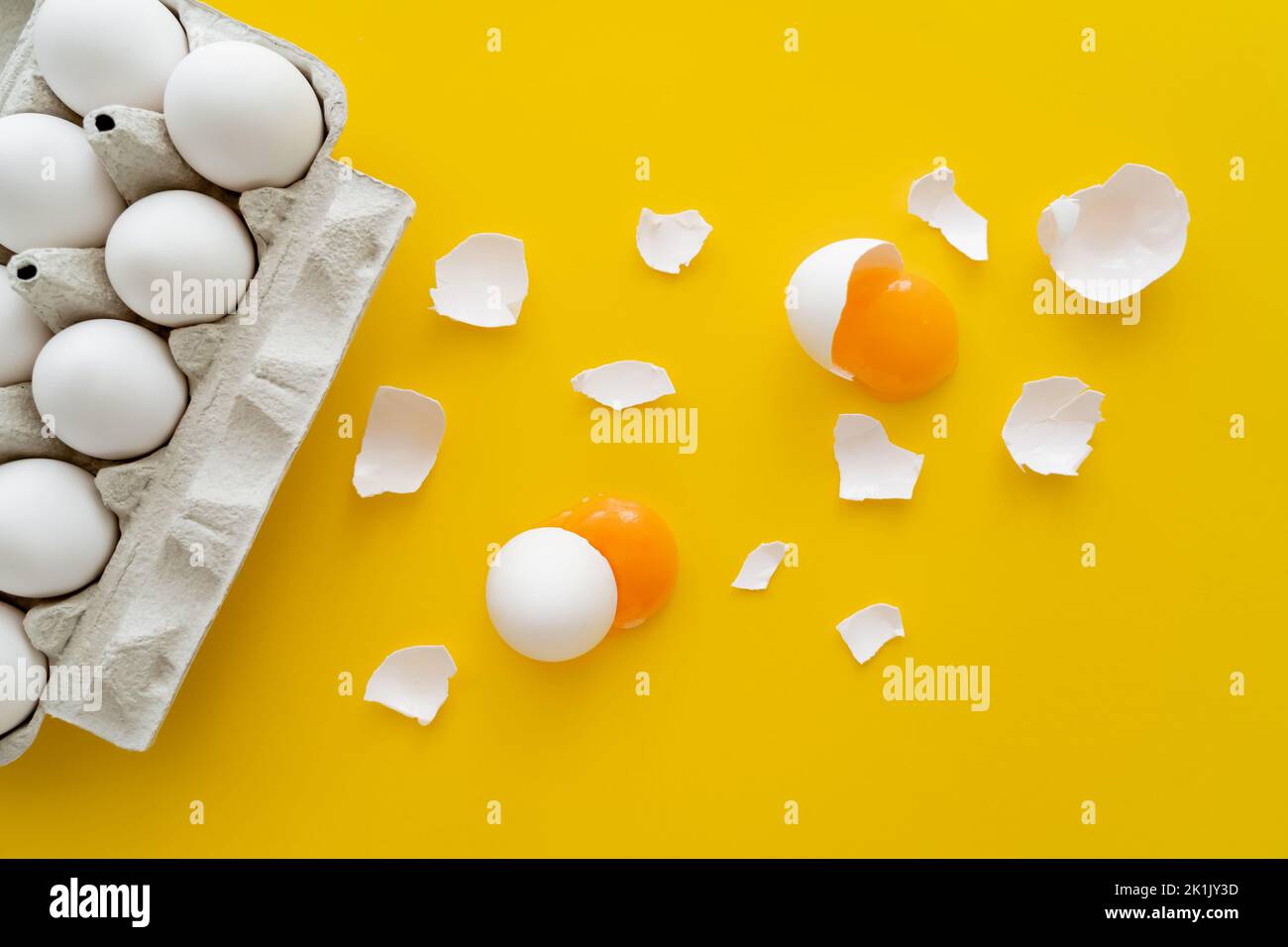 Top view of raw yolks and cracked shells near eggs in tray on yellow ...