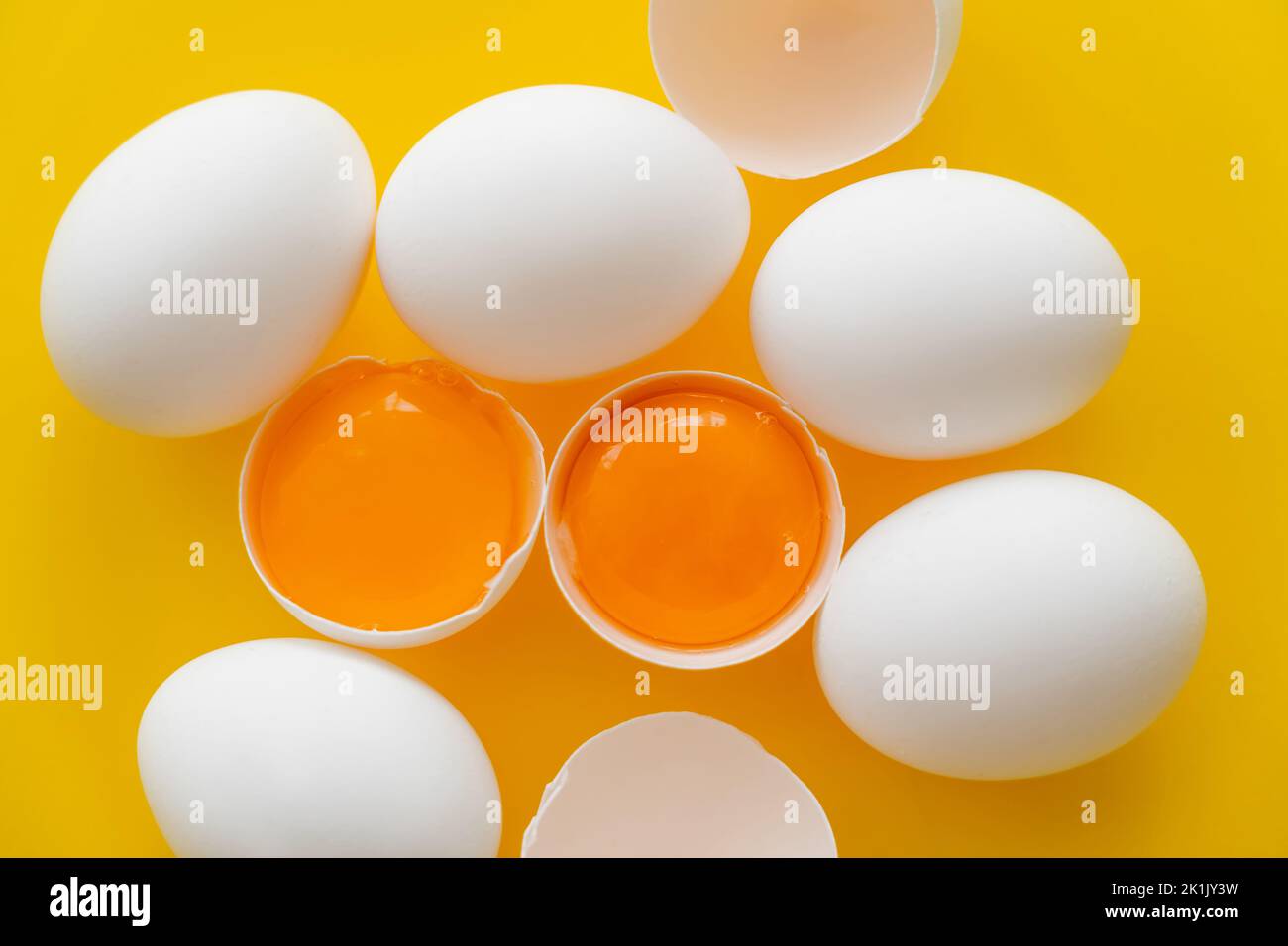 Top view of organic yolks in shells and white eggs on yellow background ...