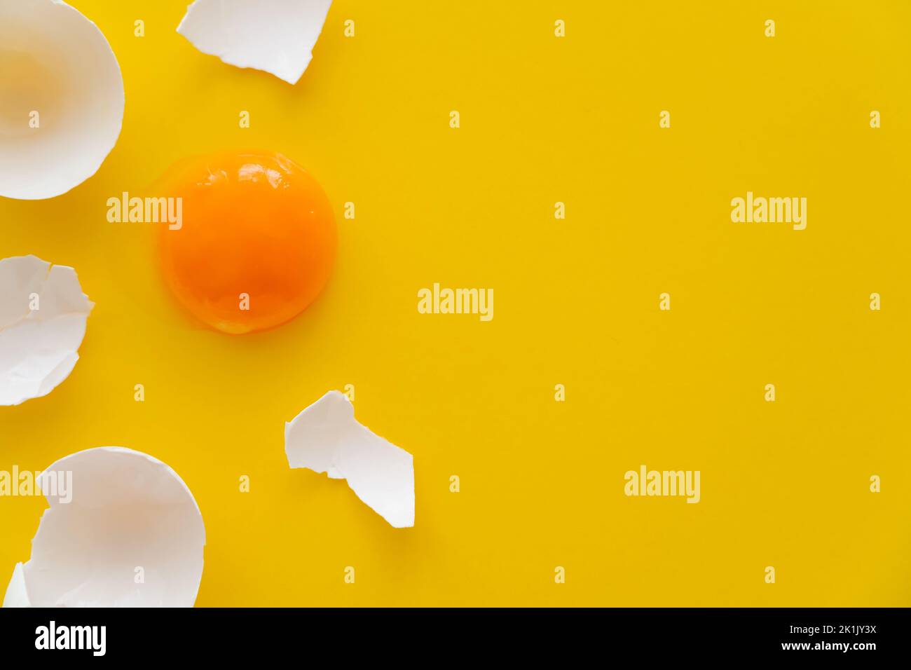 Top view of natural yolk and cracked egg shell on yellow background ...