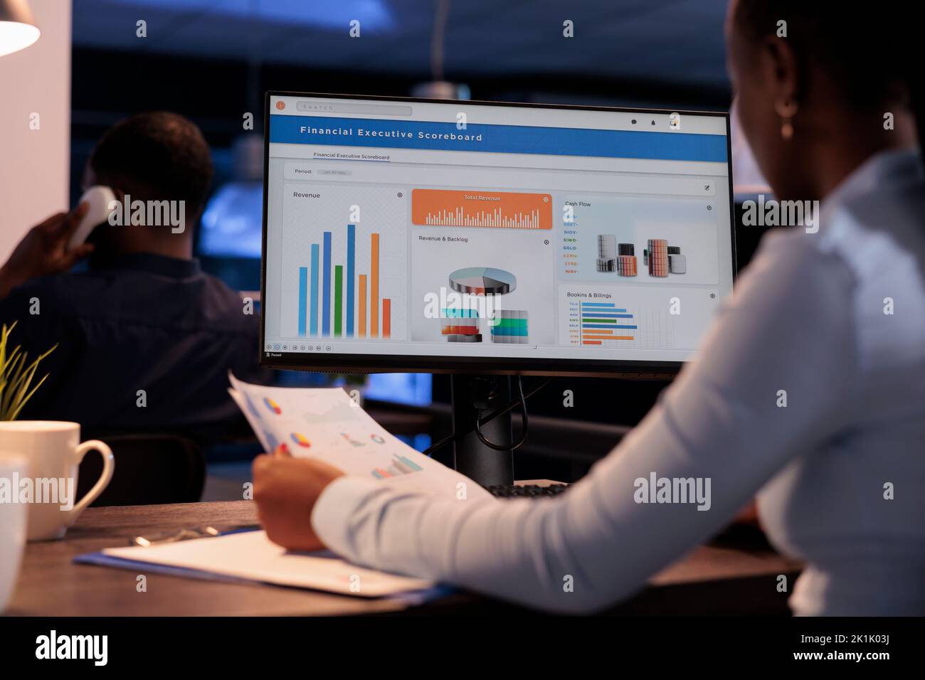 Office employee analyzing business charts on computer and documents ...