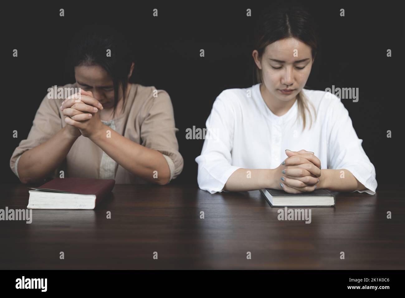 Two Christian women sit together and pray on a wooden table with ...